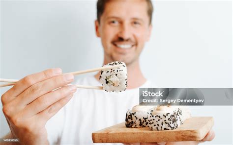 일본 요리의 초밥 전통 음식 젓가락으로 쌀 롤을 들고 카메라에 보여주는 쾌활한 미소 짓는 남자의 클로즈업 전경에 대한 선택적