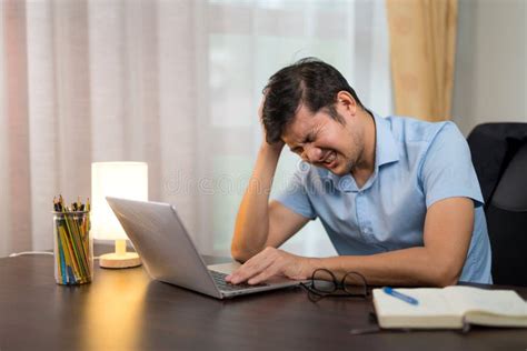 Asian Man Having Headache While Working With Laptop On His Desk At Home