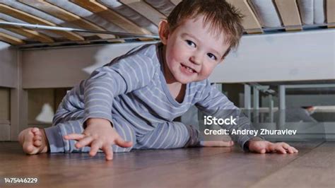 유아 아기가 기어 다니며 침대 밑에 숨어 있습니다 아이는 소파 아래로 올라가 바닥에 앉았다 사내 아이 나이 1세 8개월 전체 길이 18 23 개월에 대한 스톡 사진 및 기타