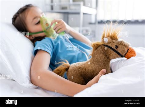 Blurred Girl With Oxygen Mask Touching Soft Toy On Bed In Clinicstock