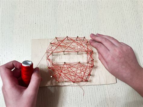 Hands Crafting Geometric String Art With Red Threads On A Wooden Board