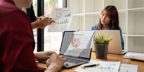 Business Team Analysis Financial Data And Discuss Strategy In Modern Office Setting With Laptops