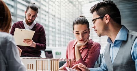 사무실에 서서 일하고 이야기하는 집 모델을 가진 젊은 건축가 그룹 사진 Unsplash의 공공 주택 이미지