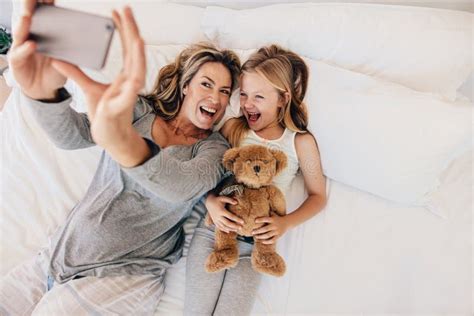 Madre Joven Que Toma El Selfie Con Su Hija En Cama Foto De Archivo