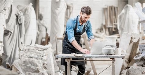 배경에 조각품이 있는 오래된 스튜디오의 작업 장소에서 노트북으로 작업하는 잘생긴 조각가 사진 Unsplash의 산업 이미지