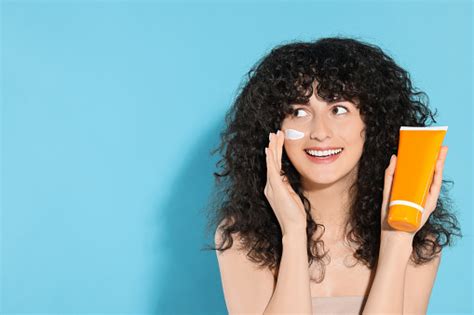 밝은 파란색 배경에 얼굴에 자외선 차단 크림을 바르고 있는 자외선 차단제 튜브를 가진 아름다운 젊은 여성 텍스트를 위한 공간