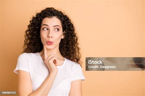 턱에 손가락을 들고 놀라운 여자의 클로즈업 사진 교활한 빈 공간을 찾고 까다로운 액션 착용 화이트 캐주얼 의상 고립 된 베이지 색 색상 배경 곱슬 머리에 대한 스톡 사진 및