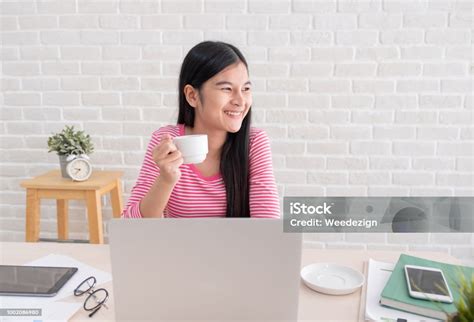 아시아 여성 프리랜서 미소와 음료와 커피 휴식 감정과 Homeworking 온라인 라이프 스타일에서 벽돌 벽에 테이블에 노트북