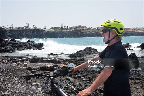 할아버지와 회색 머리 활동에서 전자 자전거 건강한 라이프 스타일 푸른 바다 물과 파도와 해안선 태양 아래에서 자전거를 즐기는 행복한 백인 사람들 건강한 생활방식에 대한 스톡