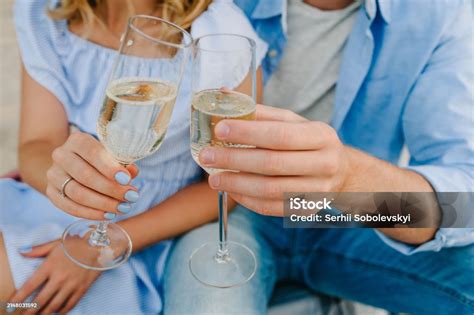 남자와 여자가 피크닉 데이트에서 안경을 들고 샴페인을 들고 있습니다 모래 바다에 피크닉 담요에 앉아있는 커플 해변 바다에서 여성과 남성이 화창한 여름날을 즐기고 있습니다