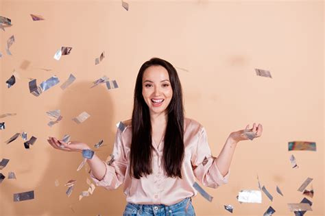 파스텔 색상 배경에 고립 된 파티에서 날아 다니는 색종이를 잡는 분홍색 셔츠를 입고 스트레이트 헤어 스타일을 입은 매우 기뻐하는 재미 있는 소녀의 사진 색종이 조각에 대한