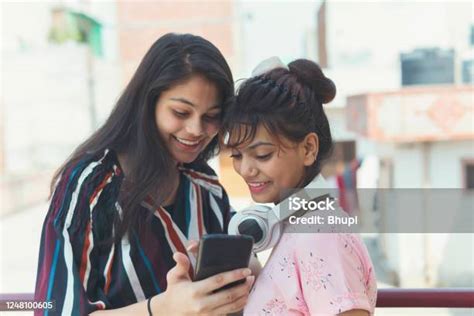 스마트 폰으로 바쁜 두 명의 아름다운 여성 친구 그리고 그녀는 발코니에 서있다 16 17 살에 대한 스톡 사진 및 기타 이미지 16 17 살 18 19세 2명