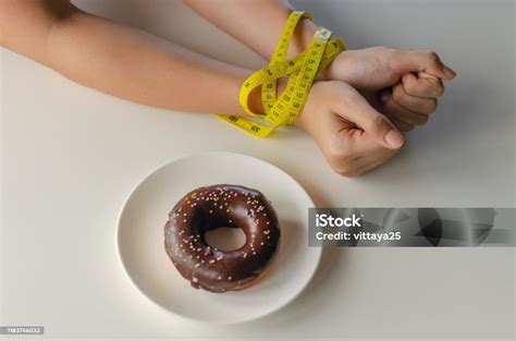 홈 오피스에서 부엌에서 책상에 노란색 측정 테이프와 맛있는 유리 초콜릿 도넛 접시로 묶여 여자 슬림 몸 손의 상단보기 정크 푸드 건강에 해로운 음식 다이어트 체중 감량 개념
