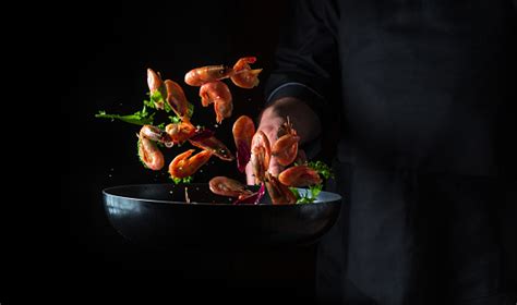 전문 요리사가 야채와 함께 팬에서 새우를 요리합니다 어두운 배경에서 해산물 건강한 채식 음식 및 음식 요리 움직임에 얼어