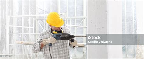 벽에 구멍을 만드는 전기 공압 드릴을 사용하는 사람 안전 노란색 하드 모자전문 건설 노동자 청력 보호 헤드폰 장갑 및 보호 안경 내부 건물 사이트 배경 파노라마 이미지에