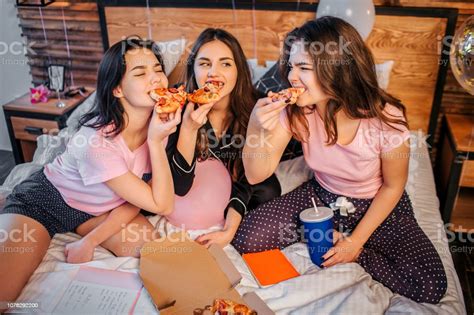 피자 조각을 물고 세 배 청소년입니다 그들은 그것을 삼 킬 배고픈 모델 착용 잠 옷 그들은 방에 있는 침대에 앉아 갈색 머리에 대한 스톡 사진 및 기타 이미지 Istock