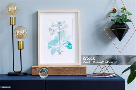 꽃 포스터와 수직 나무 프레임 테이블 램프 골드 피라미드 액세서리 회색 벽 바탕에 기하학적 냄비에 거는 식물을 모의 인테리어 감색 선반 개념입니다 0명에 대한 스톡 사진 및