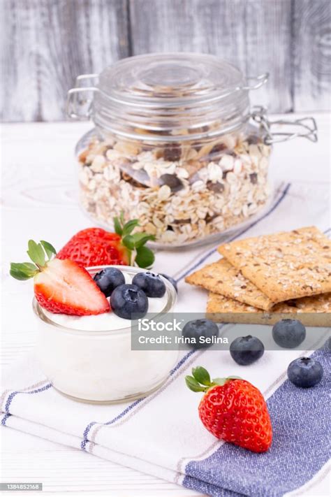 수제 요구르트와 신선한 딸기와 블루베리 뮤즐리 바삭바삭한 빵으로 소박한 스타일의 흰색 나무 테이블에 닫고 수직으로 건강한 아침