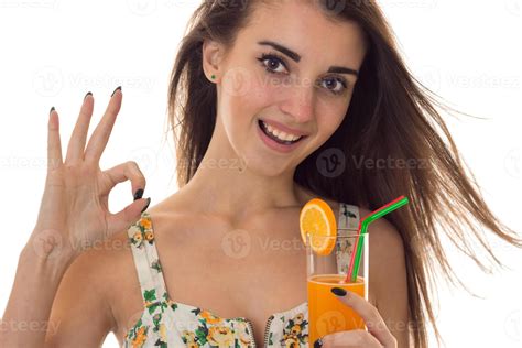 young happy brunette girl in sarafan with floral pattern drinks orange cocktail smiling on ...