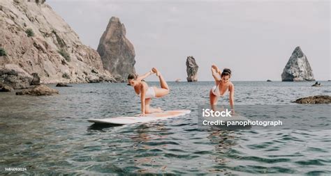 여자는 요가를 한다 패들 섭 서핑보드에서 요가 필라테스를 연습하는 행복한 스포티한 여성 바닷물에서 운동을 하는 여성 스트레칭 현대 개별 여성 힙스터 야외 여름 스포츠 활동