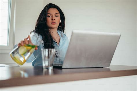 젊은 매력적인 사업가는 사무실에서 일하고 유리에 물을 붓는 동안 노트북을 사용합니다 사진 Unsplash의 우아 이미지