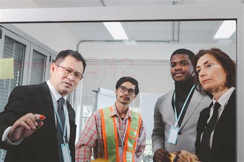 사무실에서 창조적 인 브레인 스토밍 아이디어를 위해 유리 보드에 펜 쓰기와 양복을 입은 아시아 의 수석 사업가 프로젝트 작업의 비판적 사고 결과에 대해 논의하는 기업 동료