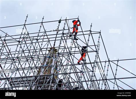 Two Skilled Workers With Safety Equipment Installing Scaffolding At The Two Skilled Workers With Safety Equipment Installing Scaffolding At The