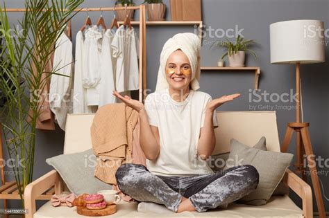 흰색 티셔츠와 수건을 머리에 쓰고 집에 있는 배경에 랙 옷을 입은 옷을 입고 웃고 있는 기뻐하는 여성의 초상화는 손바닥을 펼치고