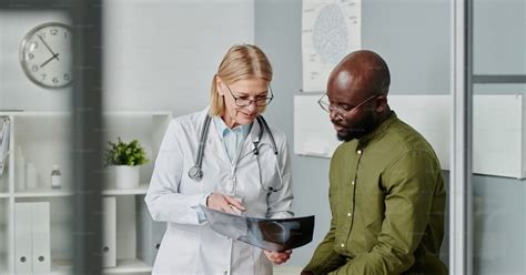 흰 코트를 입은 자신감 있는 성숙한 의사는 젊은 흑인 남성의 폐 엑스레이 이미지를 보여주고 클리닉에서 진단을 설명합니다 사진 Unsplash의 진료소 이미지