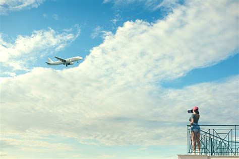 여성 사진 작가 카메라와 함께 빨간 모자에 푸른 하늘 구름과 비행기와 맞은편 발코니에 서 있다 여 자가 비행기 착륙의 사진을 찍을합니다 T 셔츠에 대한 스톡 사진 및 기타