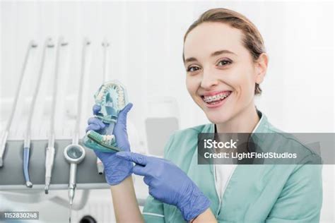 치아를 잡고 있는 치아에 중괄호를 가진 아름 다운 치과 의사는 칫 솔을 양치질 하는 방법을 보여줍니다 건강관리와 의술에 대한 스톡 사진 및 기타 이미지 Istock