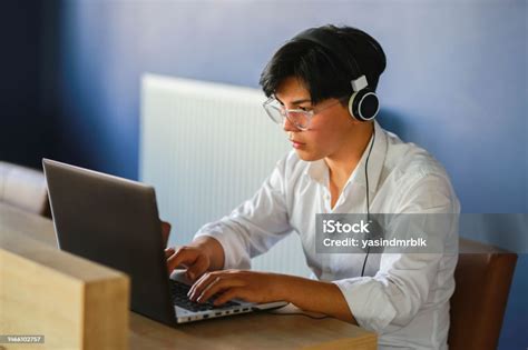 기울어진 눈을 가진 청년은 카페의 노트북에서 원격으로 하이브리드로 작동하는 헤드폰을 착용하고 있습니다 25 29세에 대한 스톡 사진 및 기타 이미지 Istock