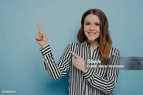 줄무늬 셔츠를 입은 귀여운 십대 소녀 빛나는 미소 광고를 위해 집게손가락으로 복사 공간을 가리키고 있다 긍정적인 여성 광고 제품 파란색 배경에 고립되어 서 있다 30 34