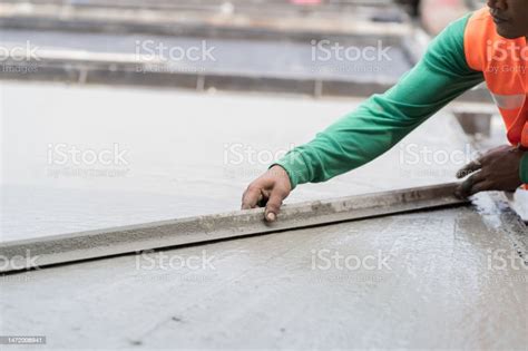 콘크리트 바닥을 매끄럽게 평평하게 하여 작업하는 건설 기술자 건설 노동자는 건설 현장에서 젖은 콘크리트를 붓는 긴 흙손을