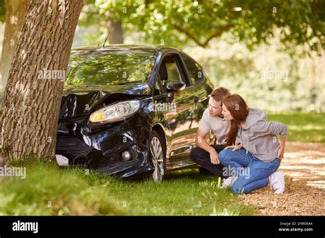 Couple Next To Car Crashed Into Tree Inspecting Accident Damage Stock Photo Alamy