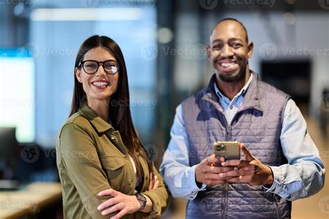 Two Cheerful Coworkers Standing Together In A Modern Office Smiling
