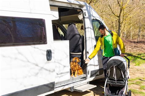 아기 경비원을 데리고 있는 아버지와 그의 개는 현대식 캠핑카 옆 숲에서 있습니다 휴가 때 가족과 함께 자연으로 여행하는 것 캠핑 생활 캠핑카에 대한 스톡 사진 및 기타