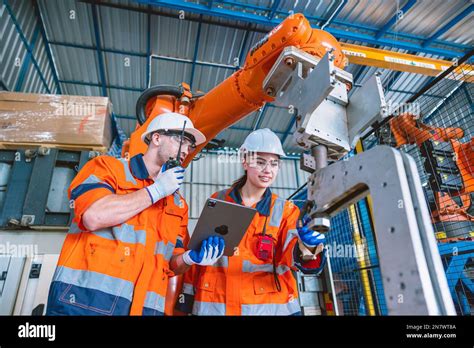 Engineer Team Worker Working With Robot Arm Assembly Machine In Modern Engineer Team Worker Working With Robot Arm Assembly Machine In Modern