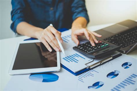 펜을 들고 계산기를 사용하여 직장책상에 있는 원형 차트 및 막대 차트와 같은 비즈니스 비용 데이터를 계산하고 분석하는 사업가 N