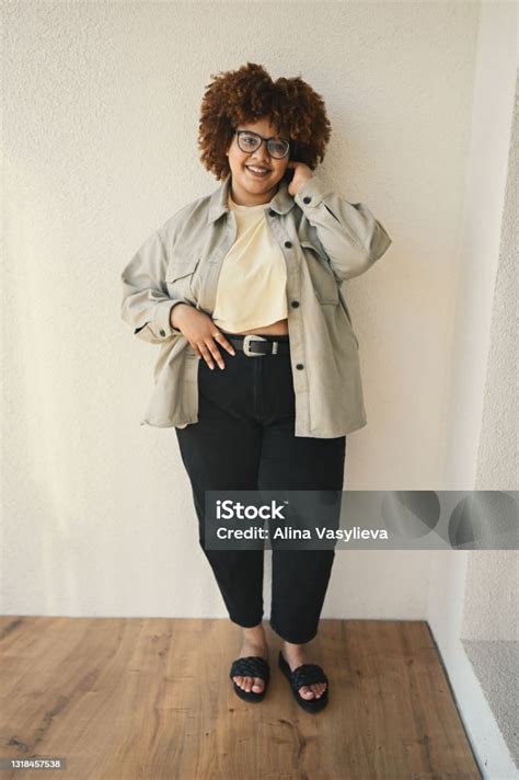 아름다운 행복한 미소 매력적인 플러스 크기 아프리카 흑인 여성 아프로 머리 포즈 베이지 색 티셔츠 청바지 베이지 색 배경에 세련된 안경 신체 불완전성 수용 체 긍정적 다양성