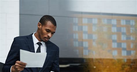 젊은 진지한 요원이 비즈니스 센터의 창가에 서서 계약서를 읽고 있습니다 사진 Unsplash의 사람 이미지