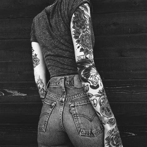 A Woman With Tattoos Standing In Front Of A Wooden Wall And Holding Her