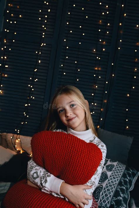 Девушка в свитере сидя на кровати и обнимая красную подушку Стоковое Изображение изображение