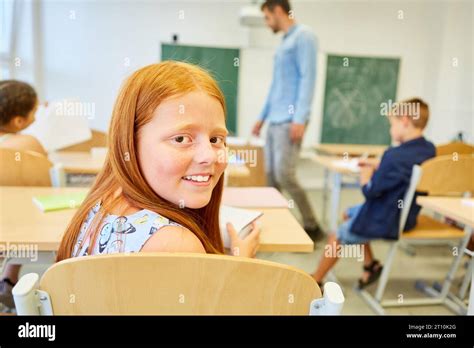 Portrait Of Smiling Redhead Female Student Sitting In Classroom Stock