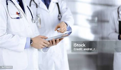 알 수없는 의사의 그룹은 병원 사무실에 서있는 동안 일부 의료 이름 기록을 확인하기 위해 컴퓨터 태블릿을 사용합니다 의사는 환자를 검사하고 도울 준비가되어 있습니다 의료