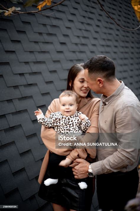 가을에는 어린 아이를 데리고 브라운과 오렌지 톤의 카페 야외 테라스에서 포옹하고 키스하는 젊은 가족 가을에는 행복한 가족이 밖으로 산책합니다 1개월에 대한 스톡 사진 및