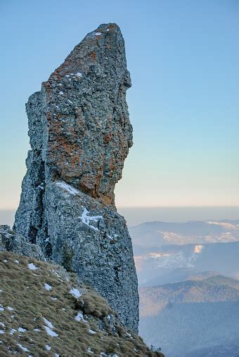 의인화 된 외관을 가진 자연 암석 절벽 안개가 자욱한 계곡과 언덕이 많은 풍경 배경 위의 산 꼭대기에 홀로 서 있습니다 극적인 겨울 풍경 조감도 0명에 대한 스톡 사진 및