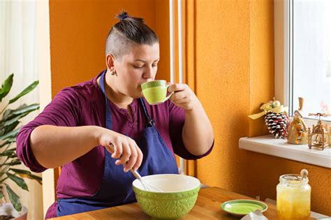 나무 테이블 뒤에 부엌에 앉아 짧은 머리와 아름 다운 젊은 여자 녹색 컵에서 차를 마시며 녹색 그릇에 재료를 혼합 그녀는 그릇으로 찾고 가정 생활에 대한 스톡 사진 및 기타