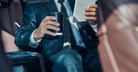 양복을 입은 우아한 남자의 자른 머리와 넥타이는 전송 중 뜨거운 음료와 터치패드 한 잔과 함께 뒤에 앉아 있다 사진