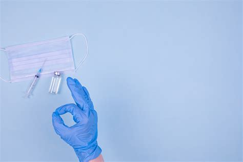 새로운 코로나바이러스에 대한 예방 접종 파란색 장갑을 낀 손은 병의 코로나바이러스 백신 접종 약물의 배경에 있는 Ok 기호와 파란색 배경의 주사기를 보여줍니다 40 44세에
